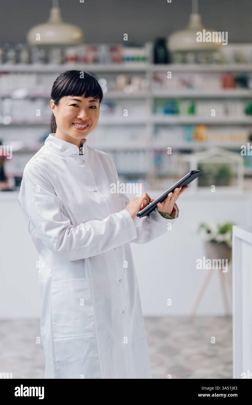 Portrait of a happy professional Japanese pharmacist standing in a drug ...