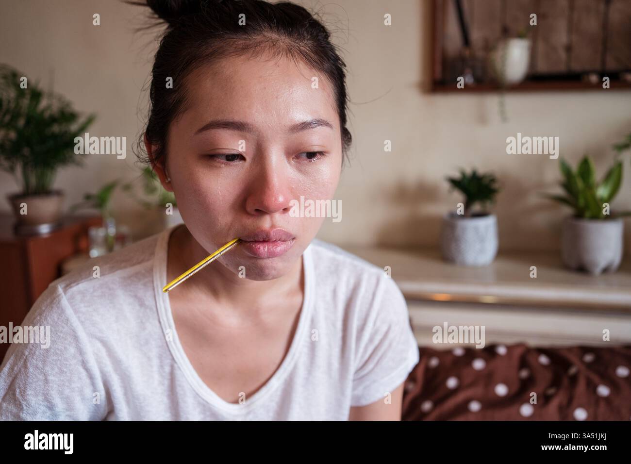 Asian woman sitting on bed at home and measuring temperature with ...