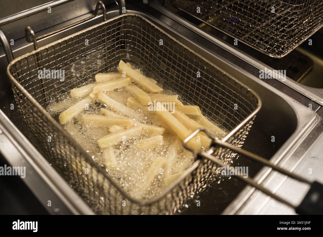 A hand uses a metal tool to lift golden french fries from a deep fryer ...
