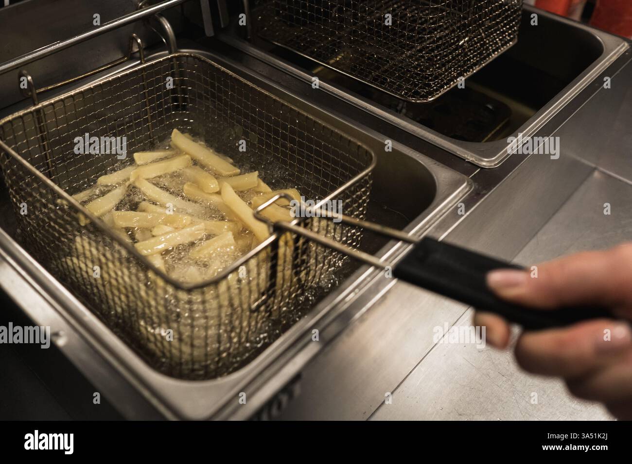 A hand uses a metal tool to lift golden french fries from a deep fryer ...