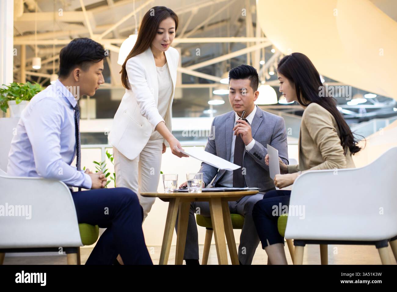 Chinese business woman putting file on table while colleagues sitting ...