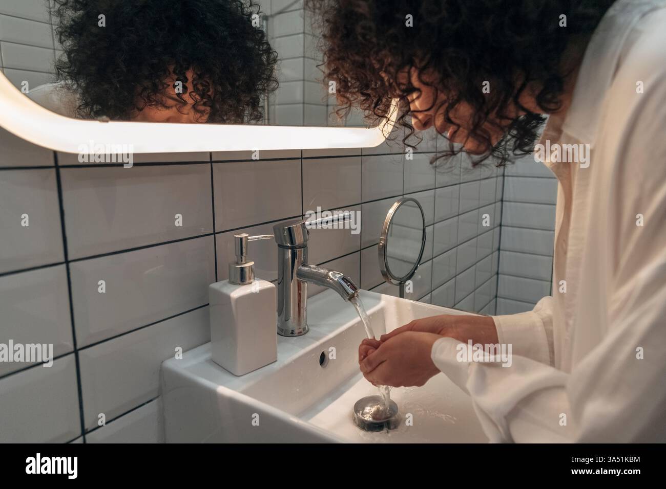 Hispanic woman washing hands and face standing near sink in the ...