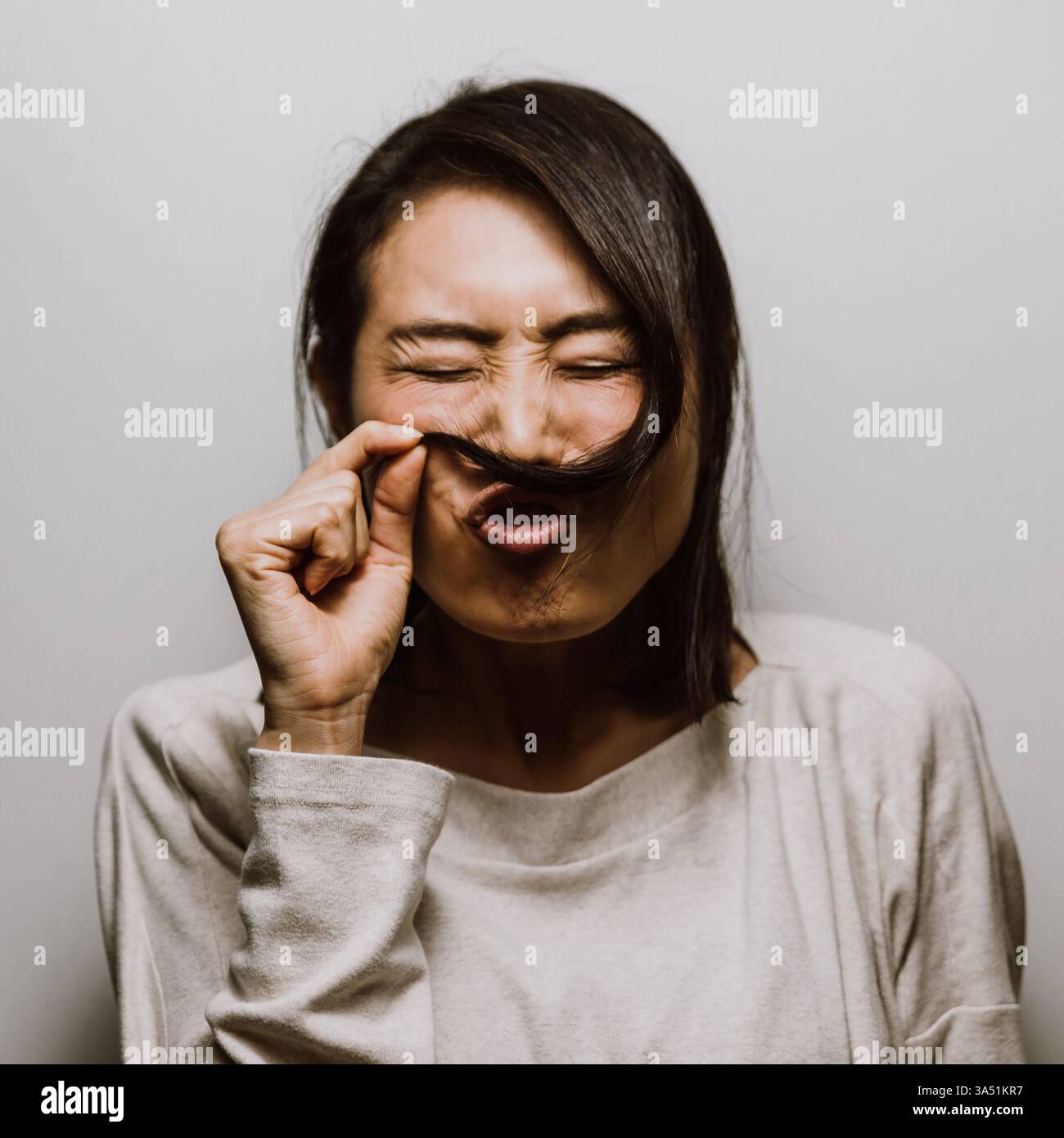 Cheerful Asian woman having fun smelling and playing with her hair ...