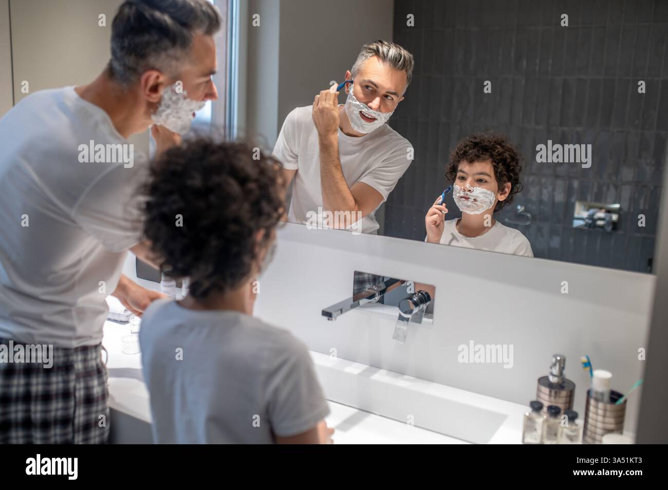 A warm domestic moment as a father teaches his son how to shave. The ...