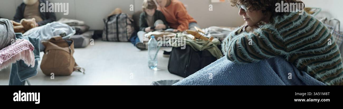 Header of lonely female refugee in striped sweater sitting on sleeper ...