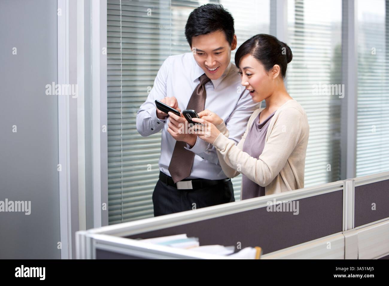 Smiling Chinese businessman and business woman using their smartphones ...