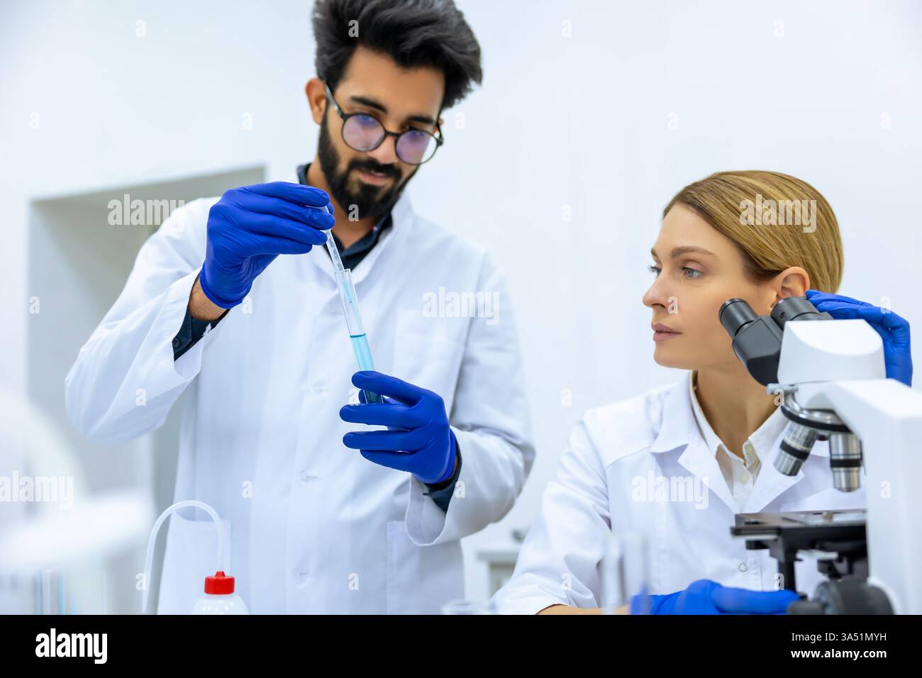 Indian male and caucasian female scientists using pipette, test tube ...