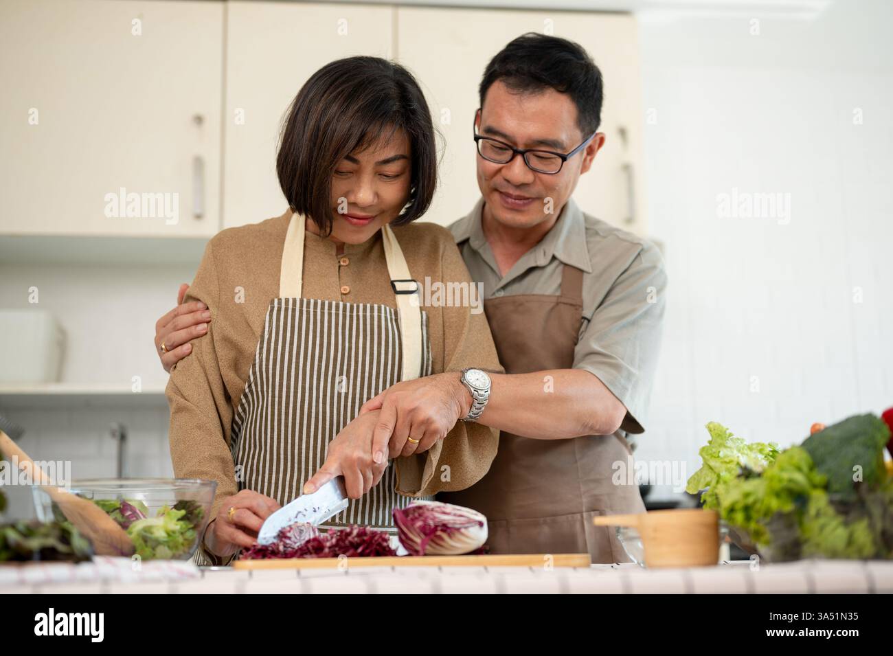 A caring Asian husband teaches and helps his wife chop vegetables ...