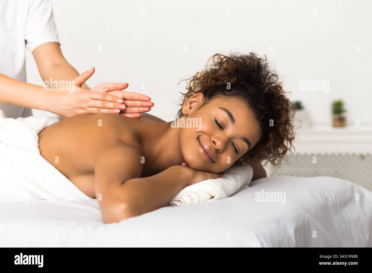 Smiling Black woman receiving back massage from female massage therapist while lying down on ...