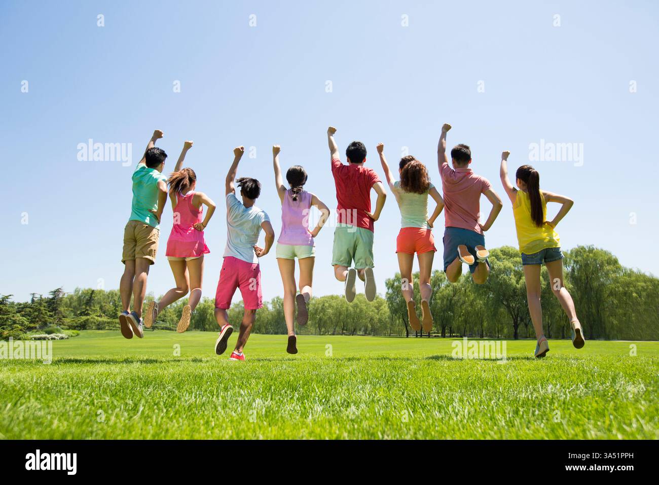 Eight cheerful Chinese young adults jump for joy across a green meadow ...