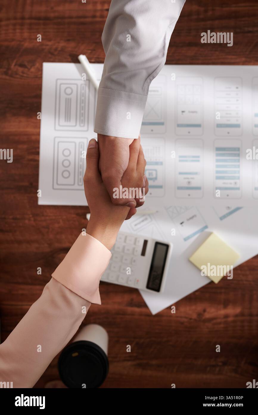 Managers shaking hands over table with project documents and mockups ...