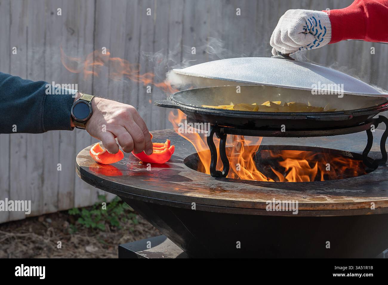 Picnic. Hands of a man cooking outdoors with friends using black hybrid ...