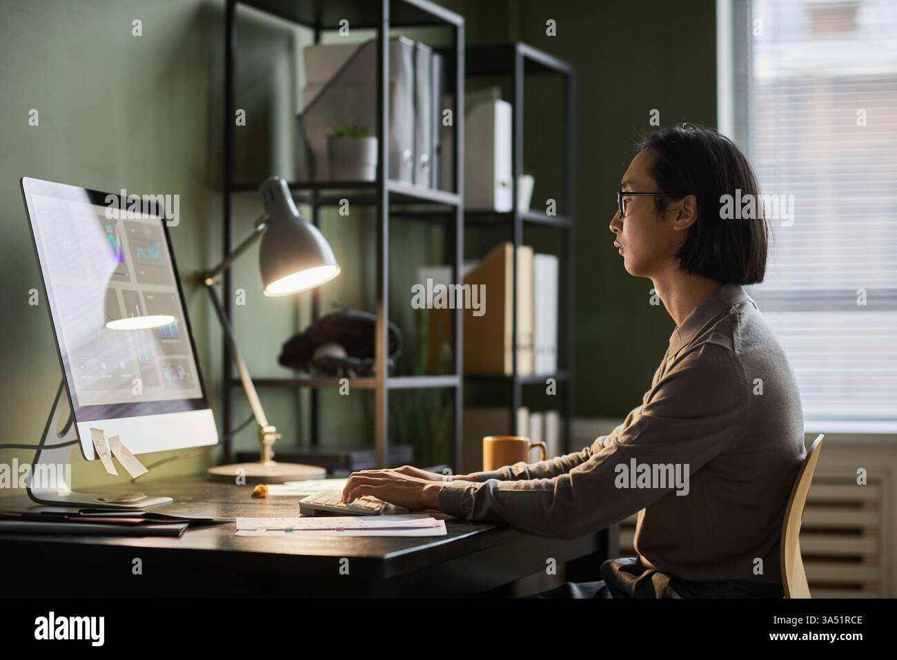 Side view portrait of Asian software designer using computer while working late at home office ...