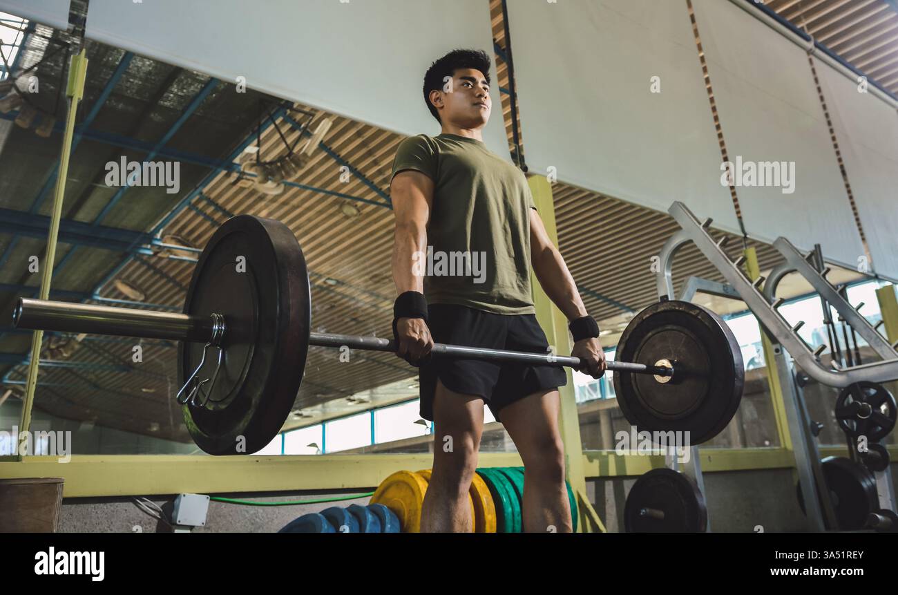 Asian male doing deadlift with heavy barbell during workout in gym ...
