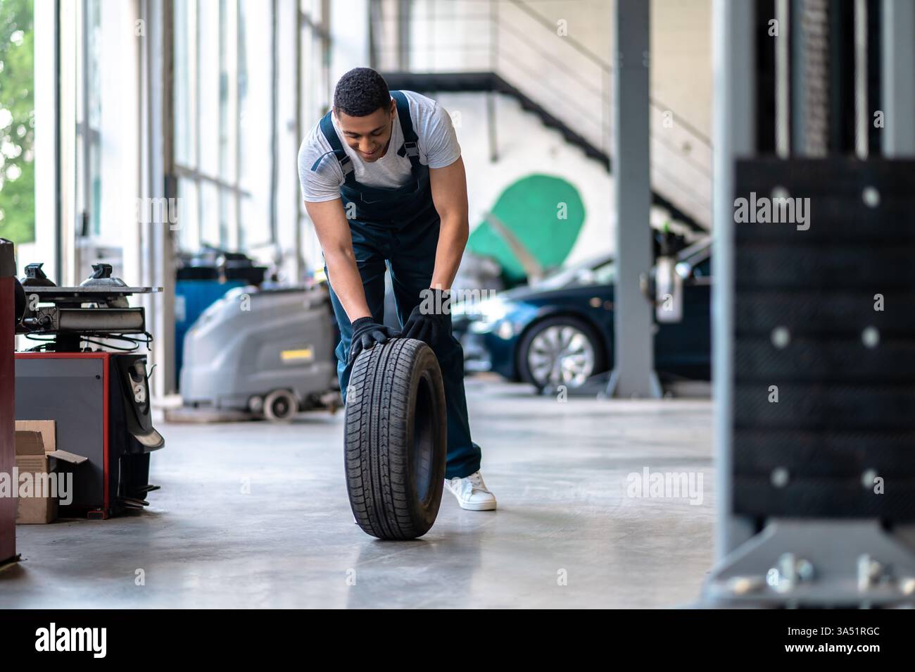 African American male mechanic rolling rubber car wheel in auto repair ...