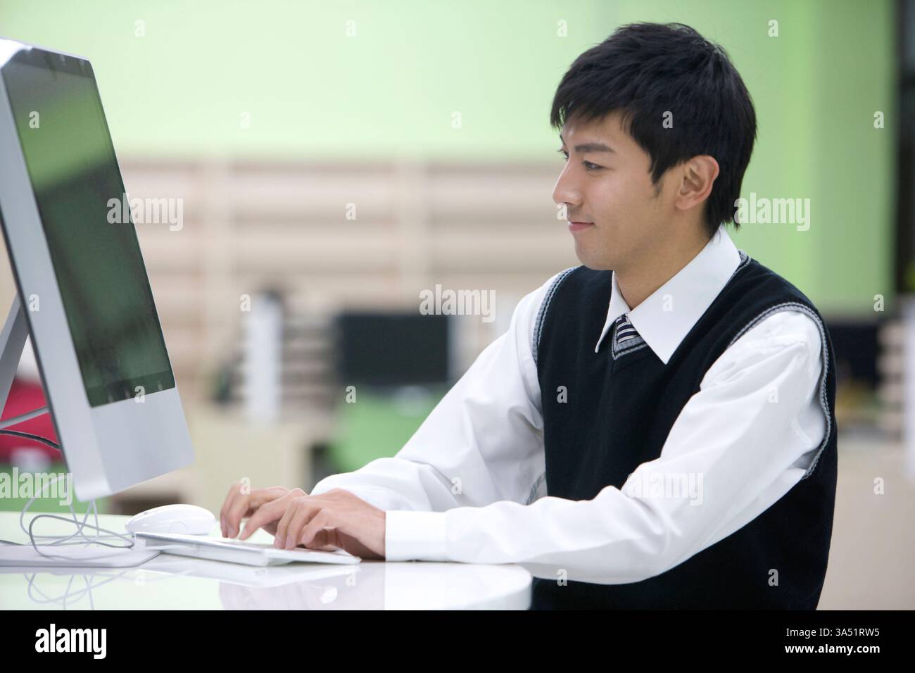 Chinese male student using computer sitting at table in computer lab ...