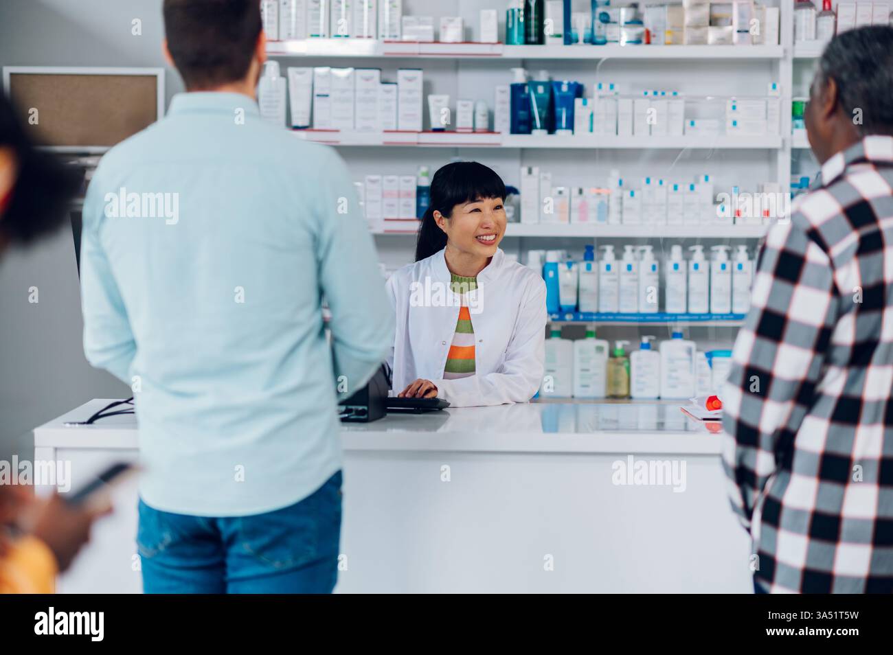 Smiling Japanese woman pharmacist typing at the counter in a pharmacy ...