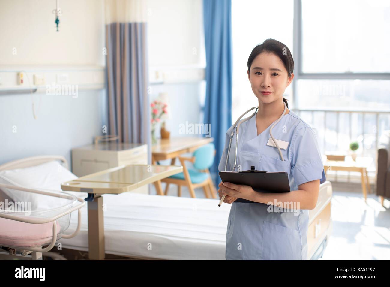 Chinese female nurse stands in a hospital room holding a clipboard ...