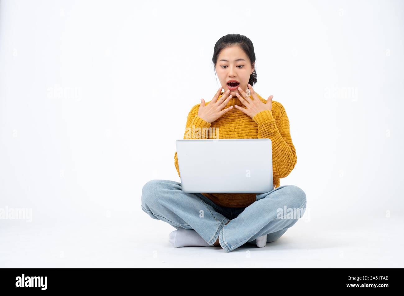 An excited and amazed Asian woman looking at her laptop screen with a ...