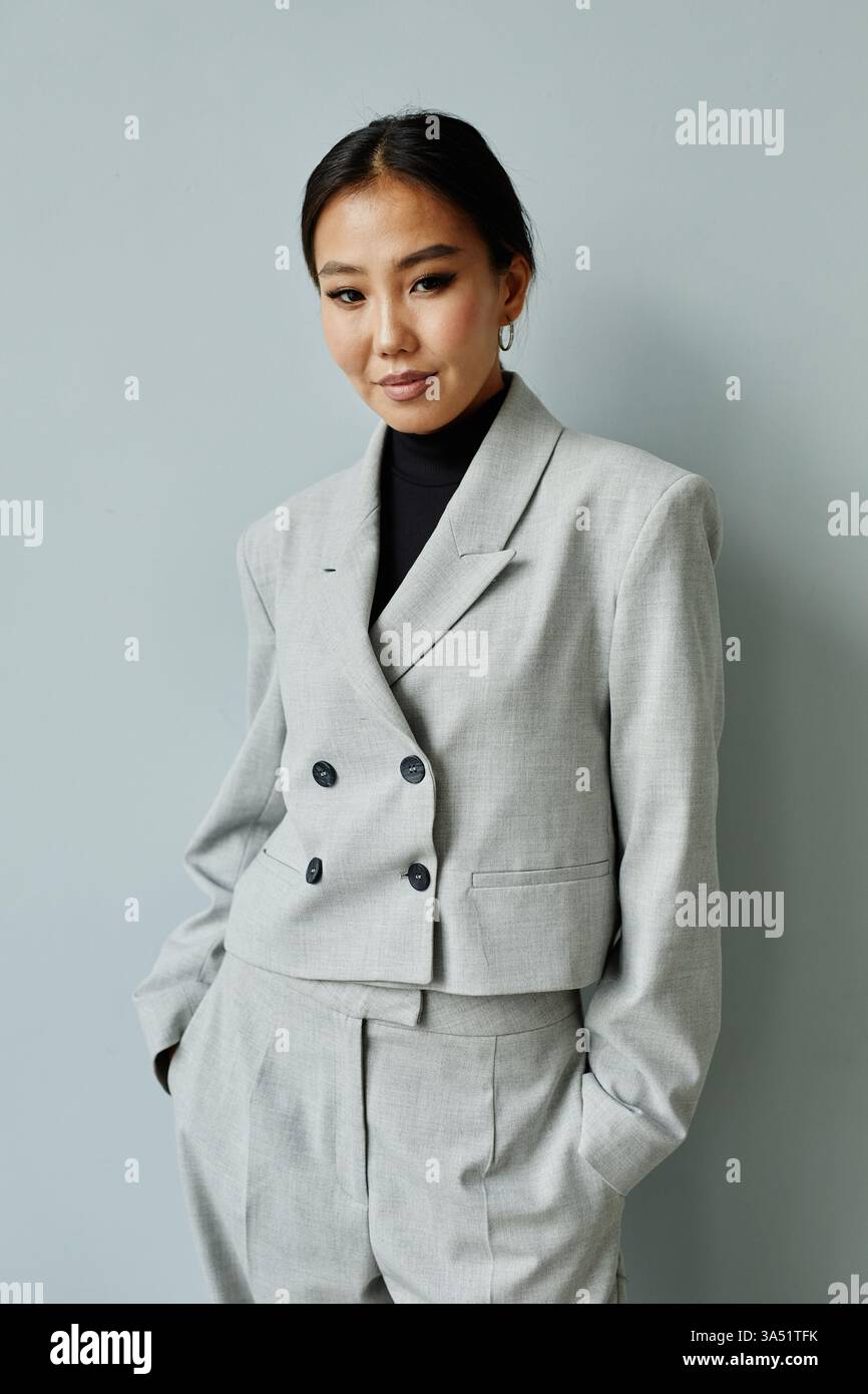 Vertical waist up portrait of beautiful Asian businesswoman wearing suit and looking at camera ...