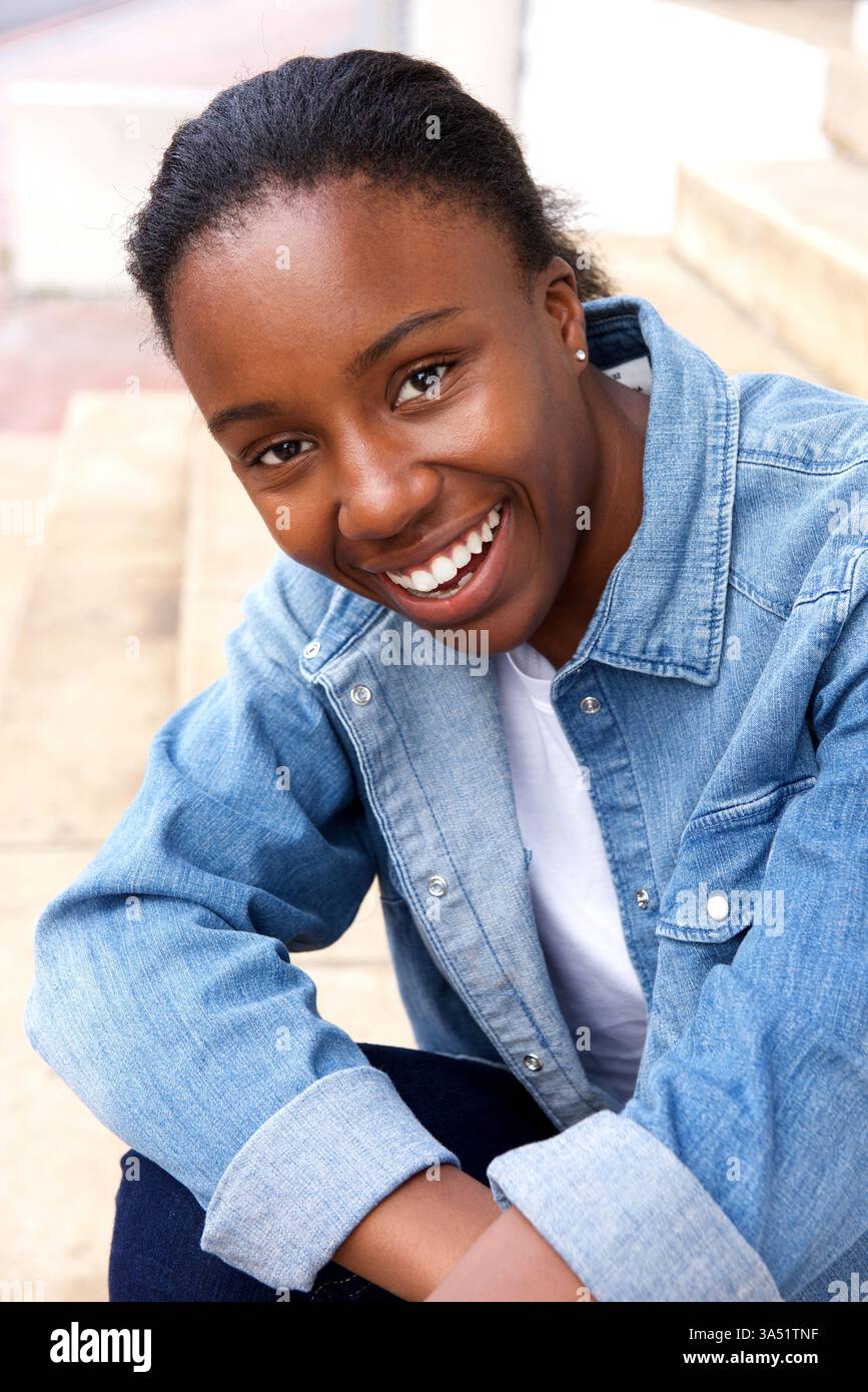 A smiling African woman sits on outdoor stairs in daytime, radiating ...