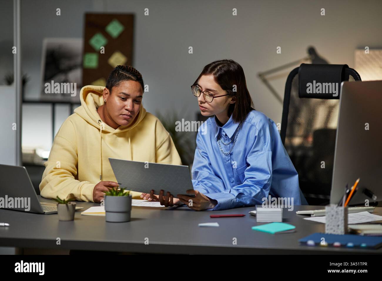 Front view portrait of two young women discussing documentation while working late at night in ...