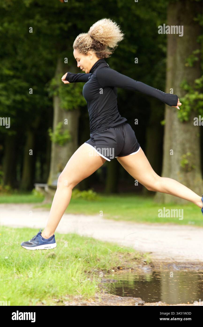 Portrait of a sporty Black woman jumping over a puddle outdoors. The ...