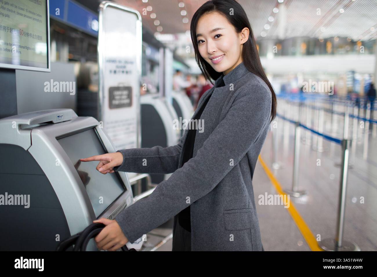 Smiling Chinese business woman standing while using ticket machine in ...
