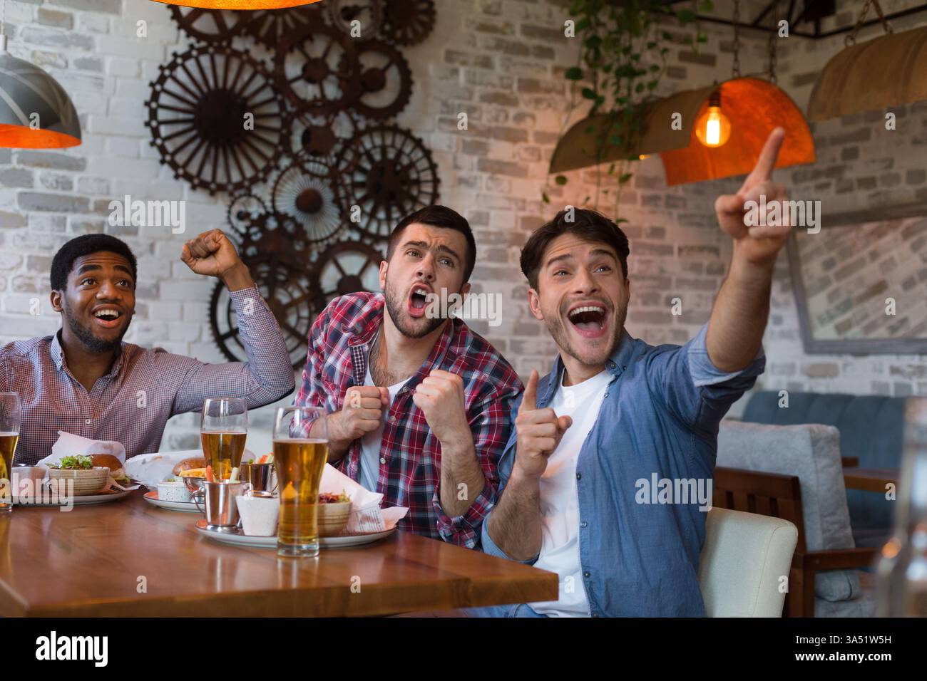 A group of friends watches a football game on TV in a bar, sharing ...
