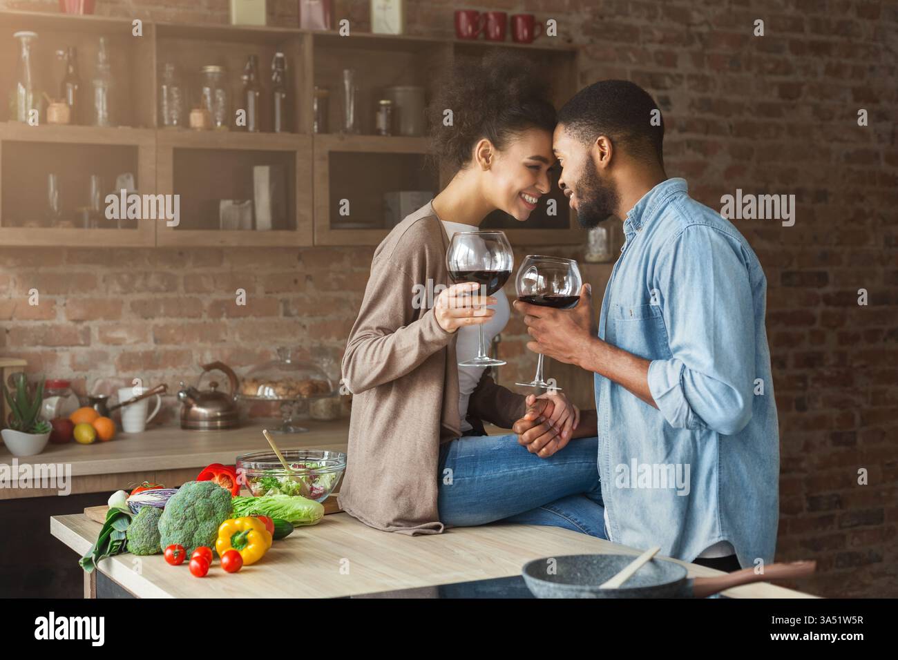 Romantic couple toasting each other in kitchen with glasses of red wine ...