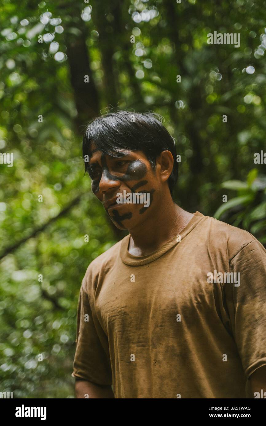 Serious male of tribe with painted face standing in green tropical ...