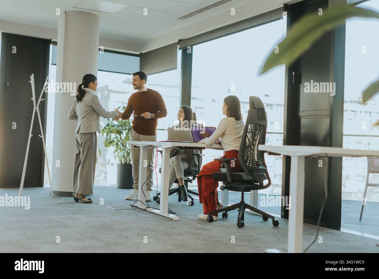 A group of four business professionals engages in a dynamic meeting at ...