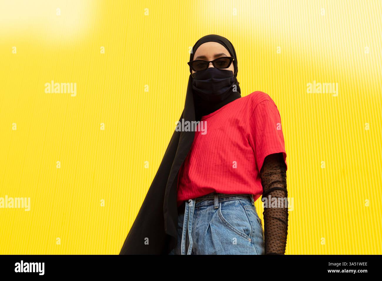 Arab woman wearing hijab and face mask standing against colorful wall ...
