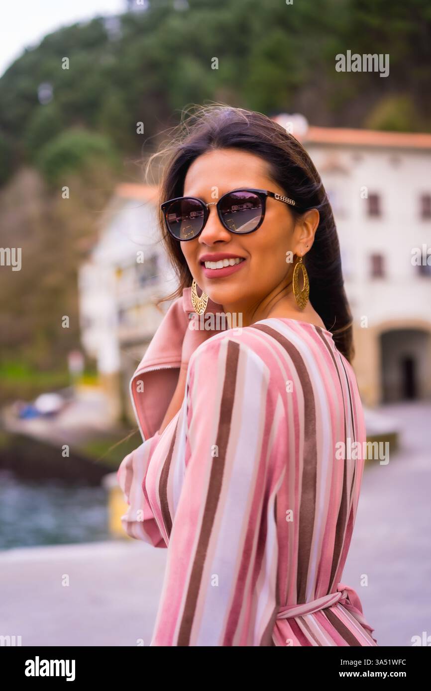 Portrait of a young Latin woman in a pink dress and sunglasses enjoying ...