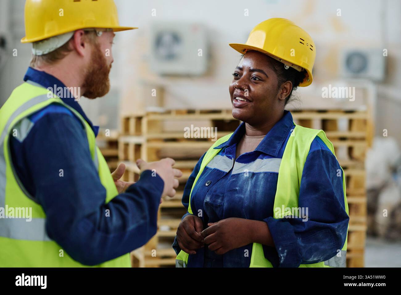 Two young intercultural engineers in workwear discussing features of ...