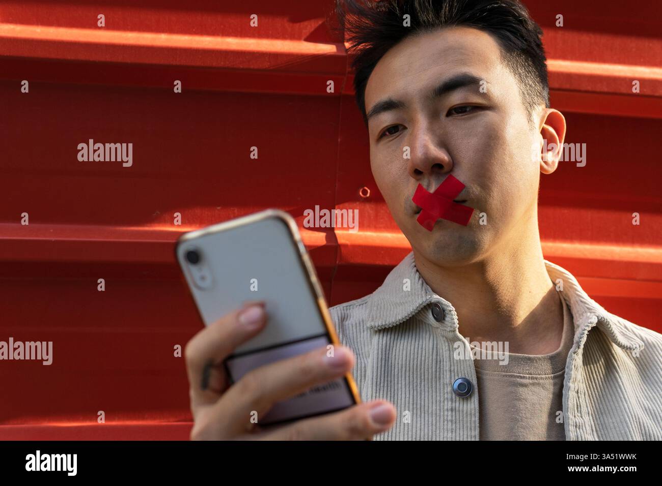 Asian man with red tape on lips using mobile phone Stock Photo - Alamy