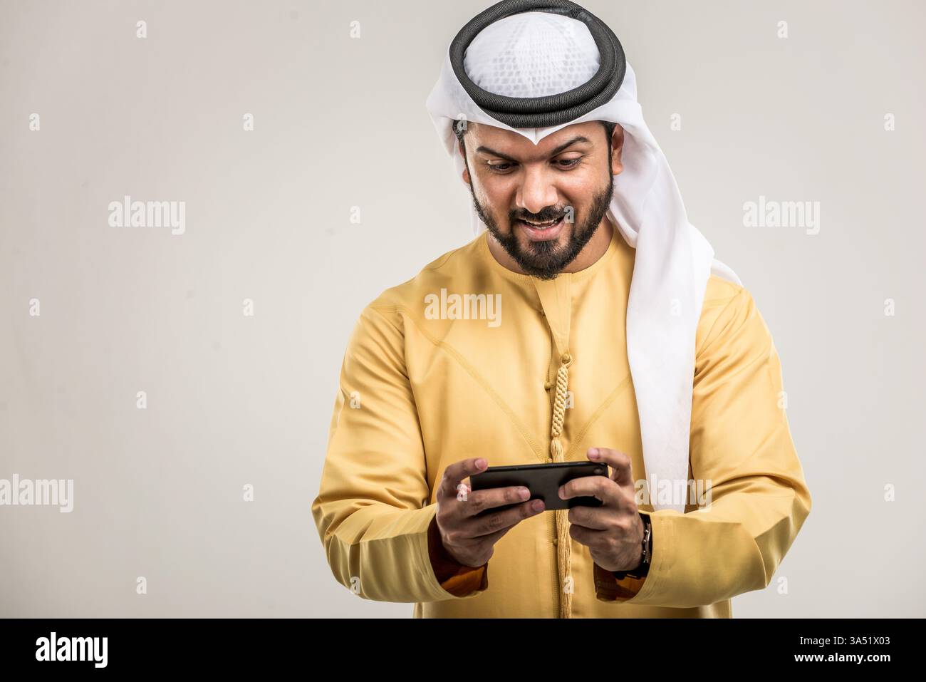 Smiling Middle Eastern man using smartphone standing against gray ...