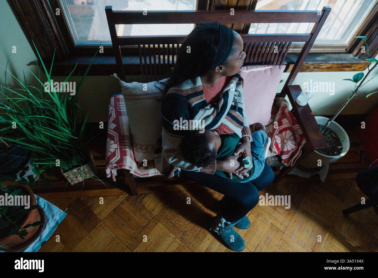 Baby with eyes closed latched onto mother holding pacifier sitting on ...