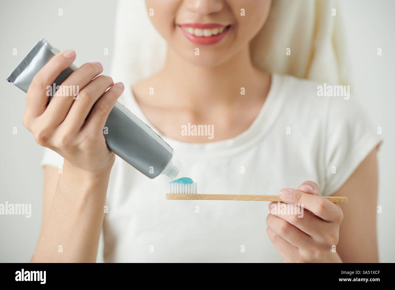 Smiling Asian woman wearing white shirt holding toothpaste and ...