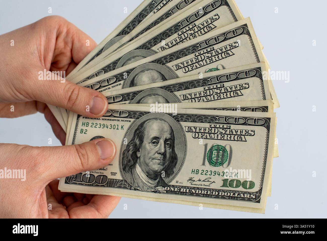 Hand holding spread of US hundred-dollar banknotes, representing ...