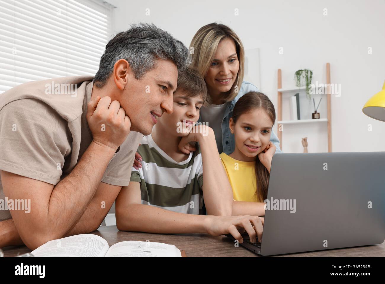 Parents and their children doing homework with laptop at table indoors ...