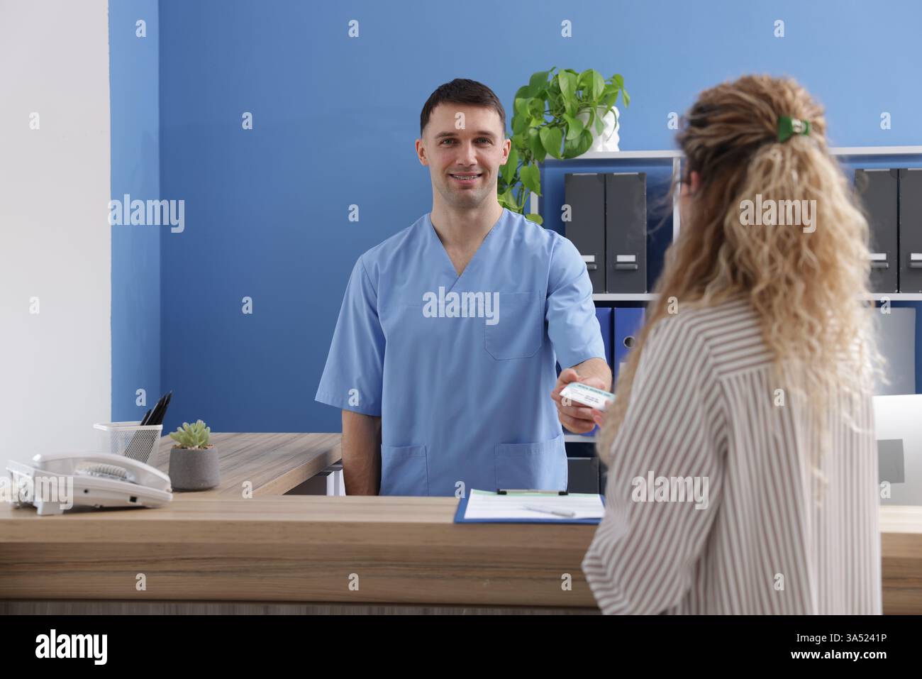 Patient giving medical insurance card to smiling receptionist in clinic ...