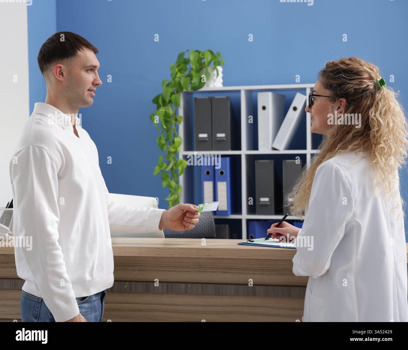 Smiling patient giving medical insurance card to receptionist in clinic ...