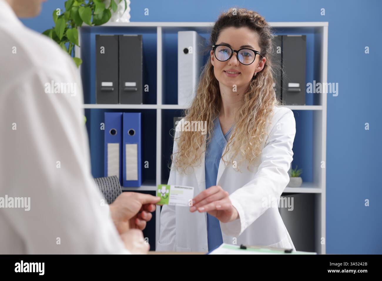 Patient giving medical insurance card to smiling receptionist in clinic ...
