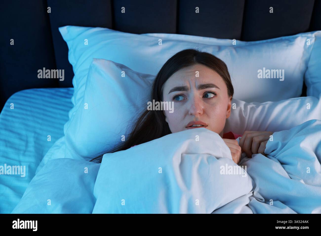 Fear of darkness. Scared young woman lying on bed in room at night Stock Photo - Alamy