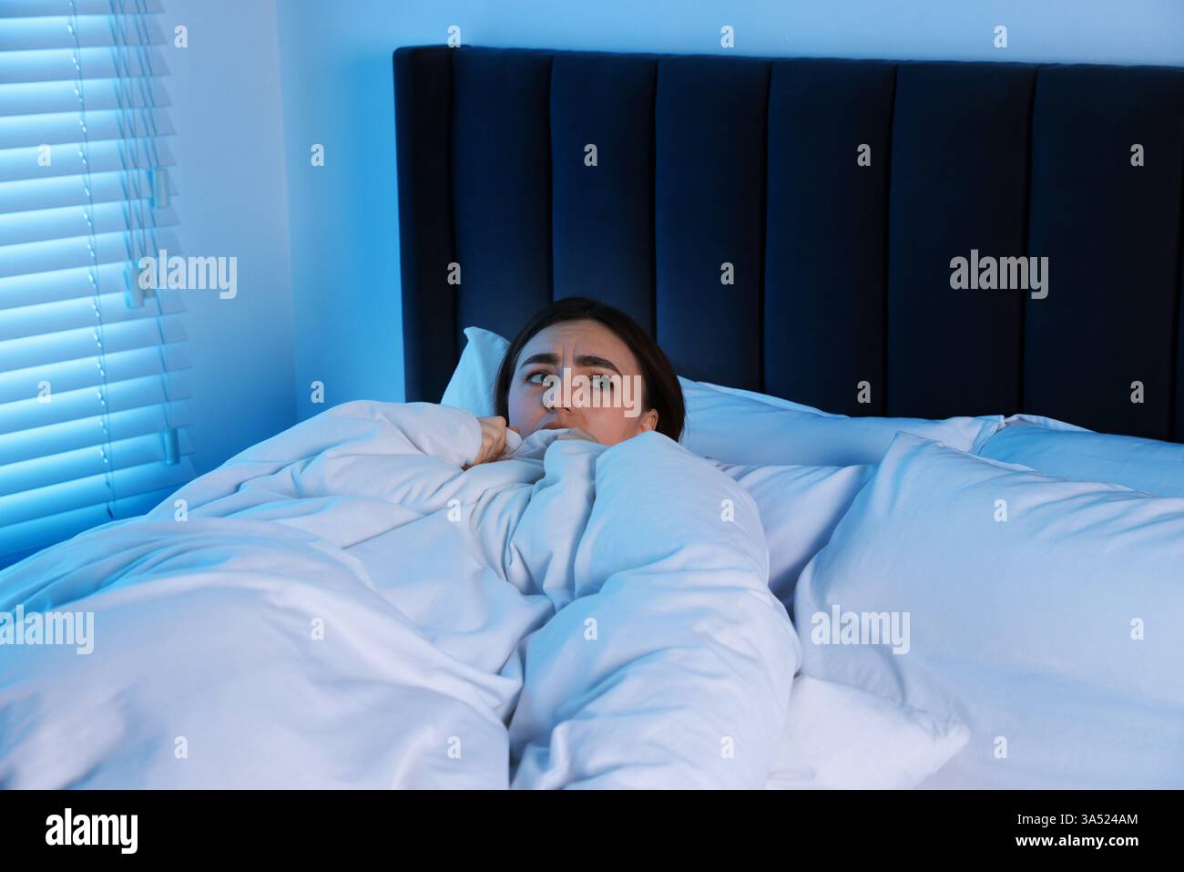 Fear of darkness. Scared young woman lying on bed in room at night ...