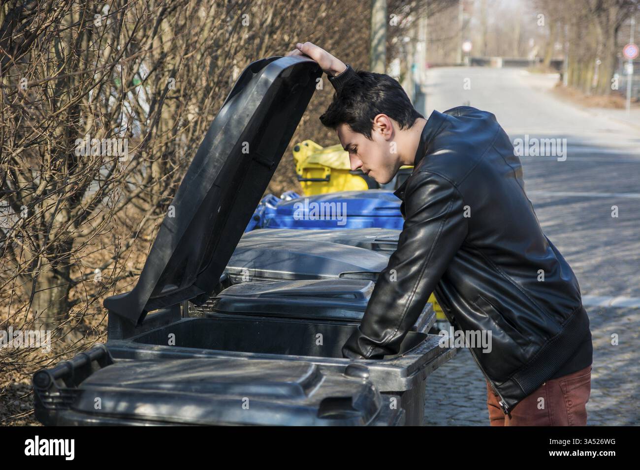 Attractive young man putting out rubbish standing with the lid up on a ...
