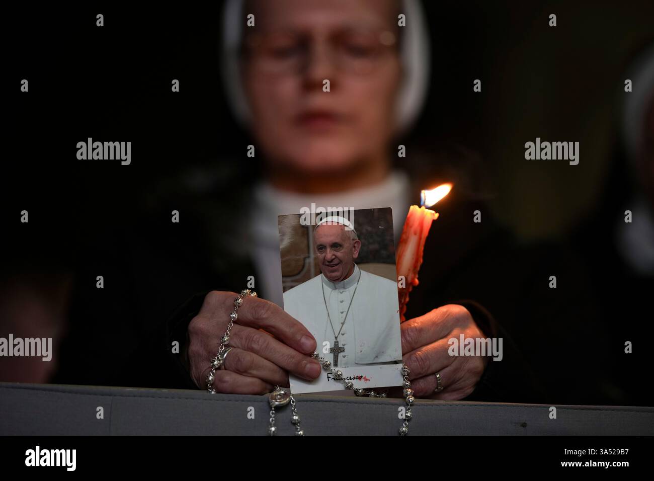 A nun holds a candle and an image of Pope Francis during a rosary ...
