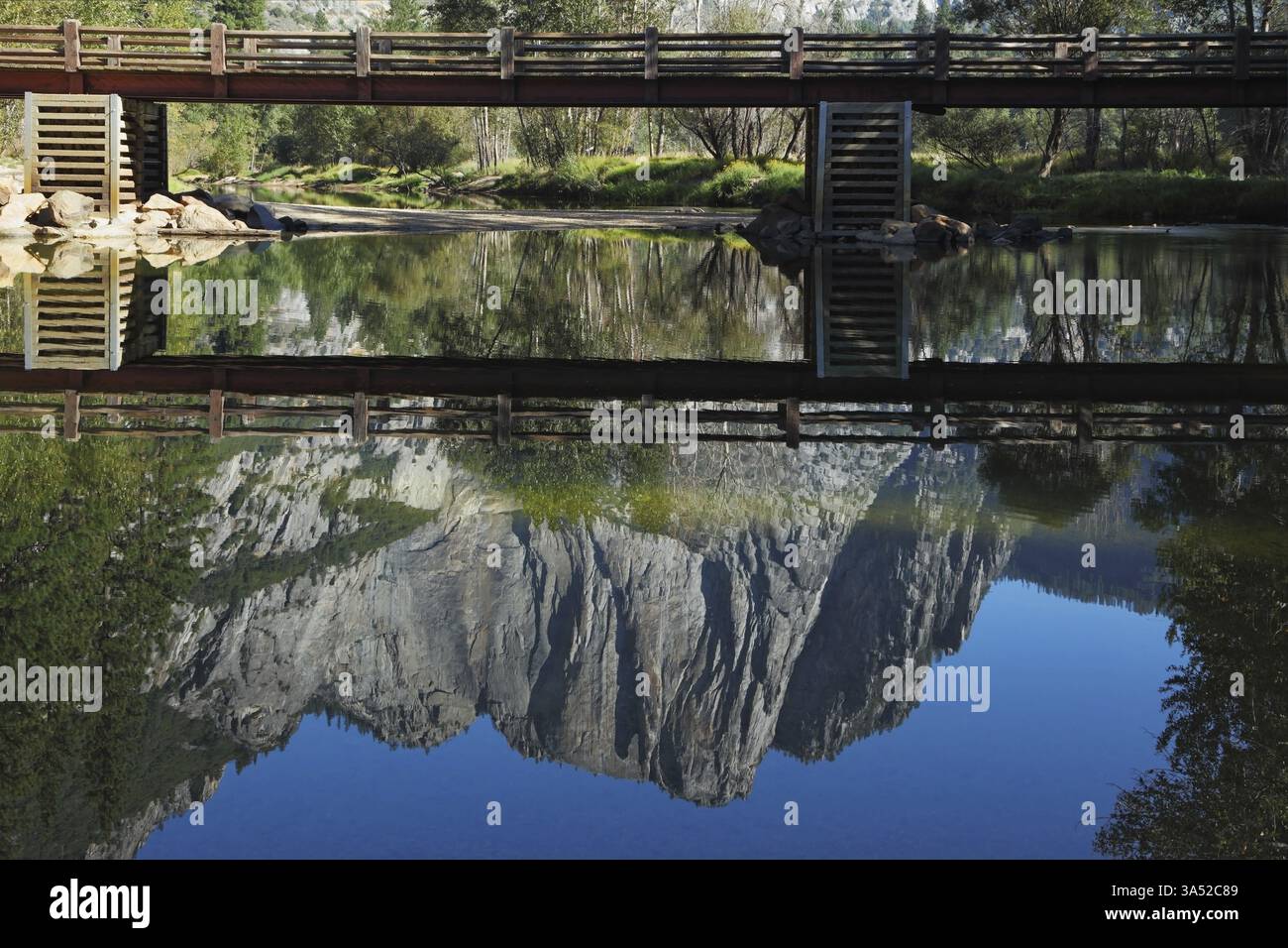 Wooden footbridge over the Merced River in Yosemite Park. In the still ...