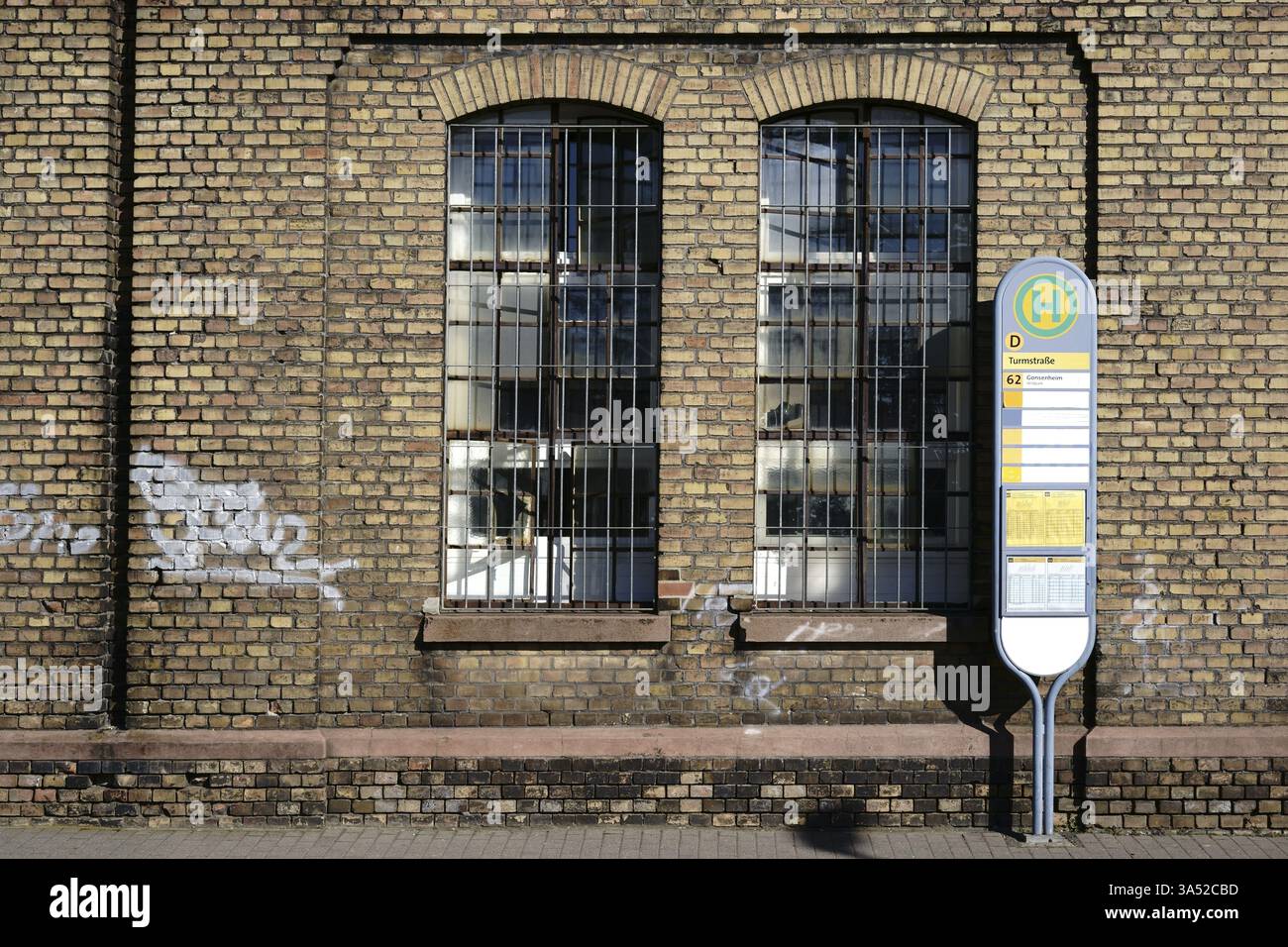 A bus stop sign stands in front of the brick wall of a disused ...